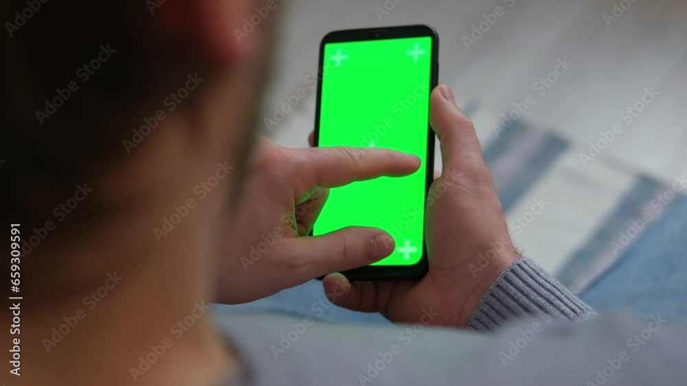 Young man sitting at home holding smartphone greenscreen mock-up in ...