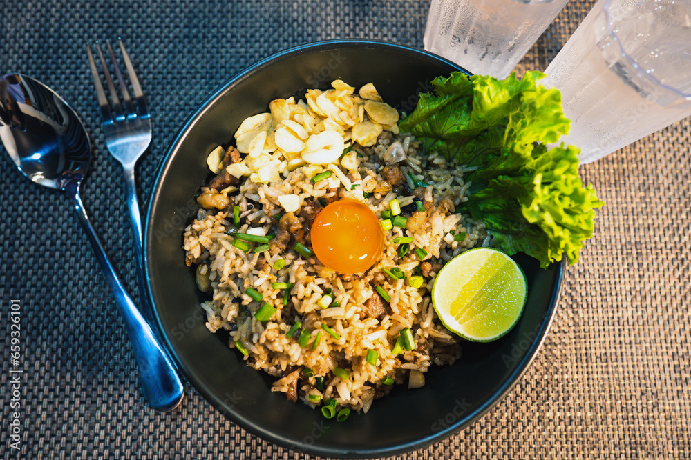 Fried rice with undercooked egg yolk in a black bowl with spoon and ...