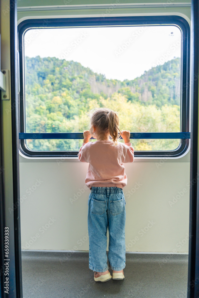 Beautiful little girl looking out train window outside, while it moving ...