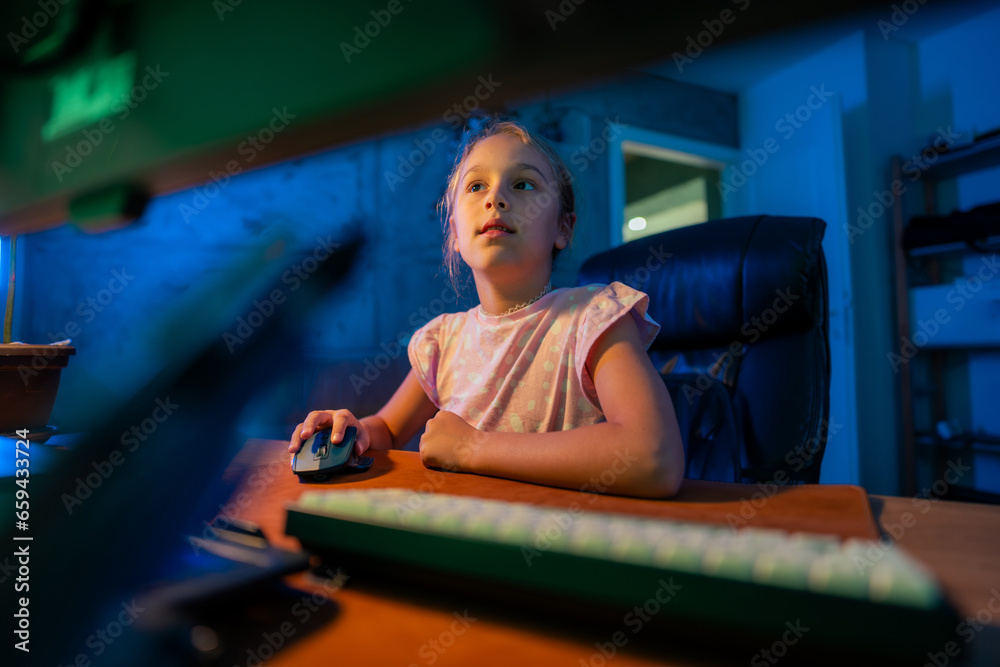 A child sitting in front of a computer screen in a dimly lit room ...