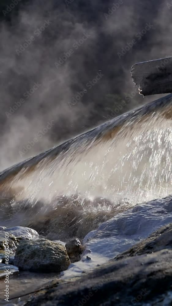 Vertical video of a stream of hot mineral water flowing onto stones ...