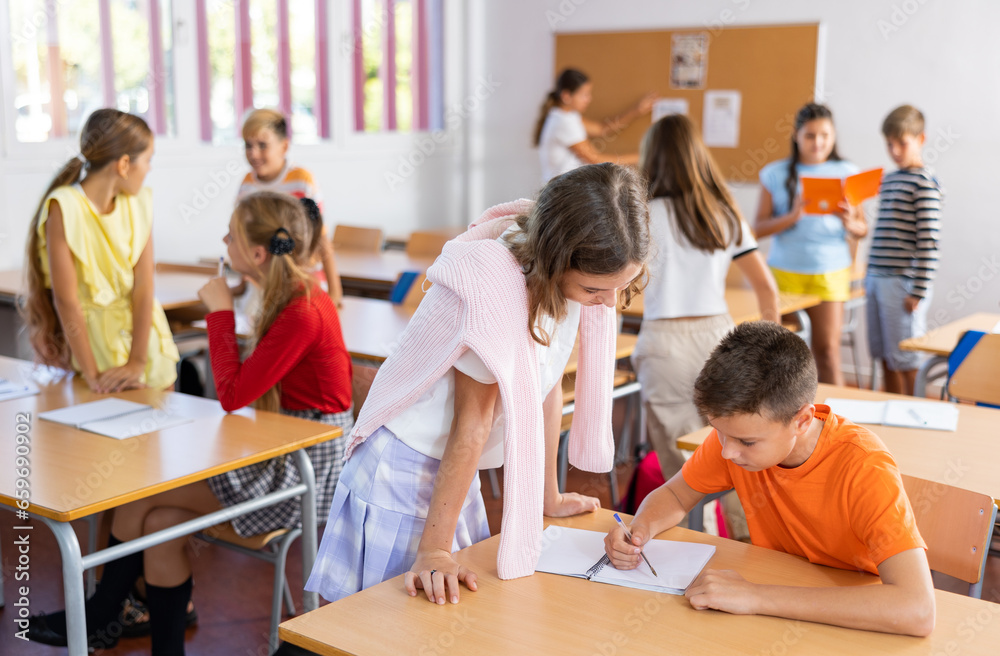 Positive friendly tween girl helping classmate sitting at school desk ...