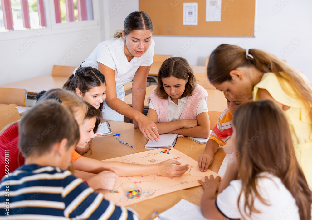 Teacher and group of kids playing board game in school after lessons ...