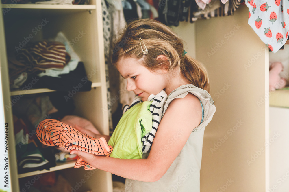 Little school girl standing by wardrobe with clothes. Preschool child ...