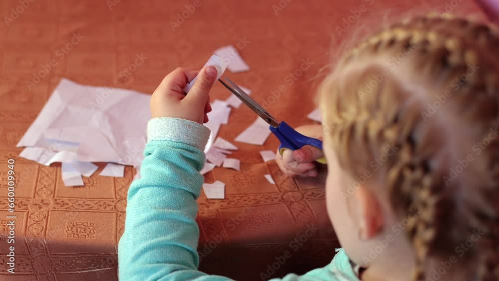 A child cuts paper with scissors. A little girl is sitting and cutting ...