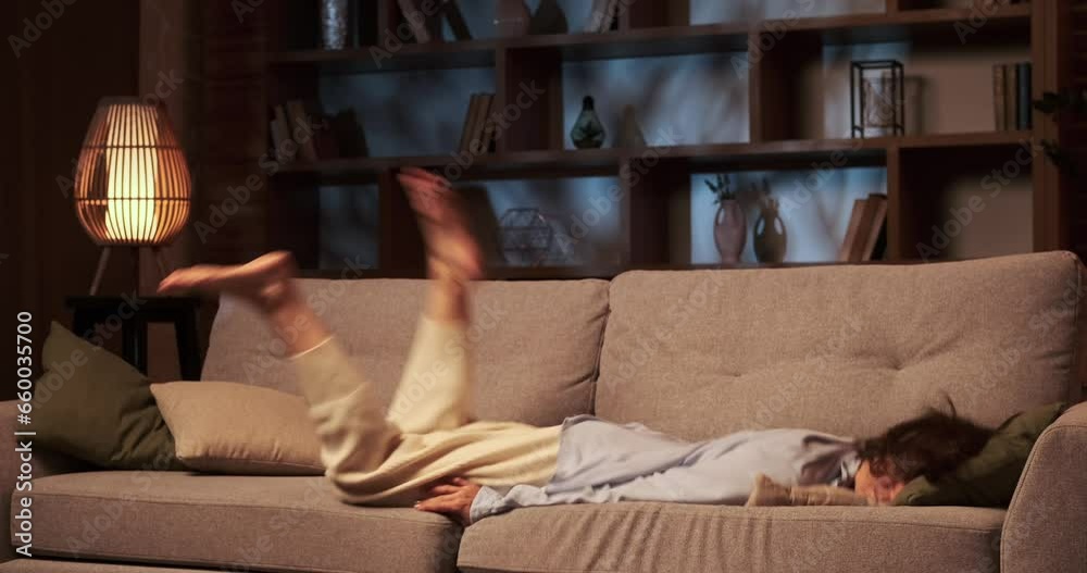 Woman collapses onto the sofa in the living room, her body sinking into ...