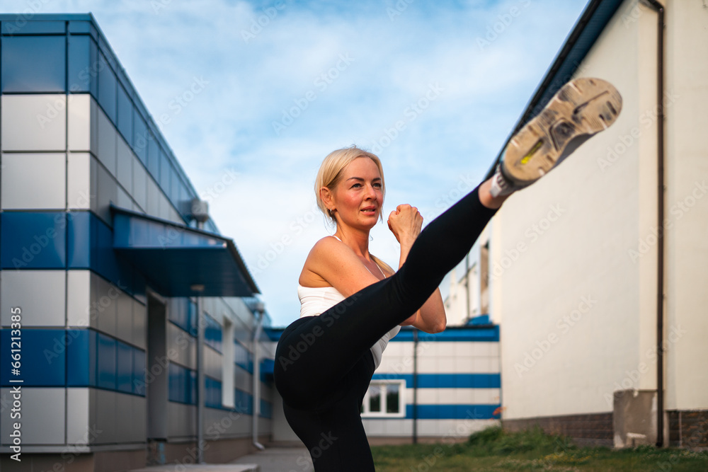 Adult beautiful blonde woman doing box kicks exercises workout outdoors ...