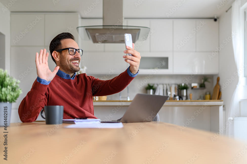 Happy businessman with laptop on desk waving hand while video calling ...