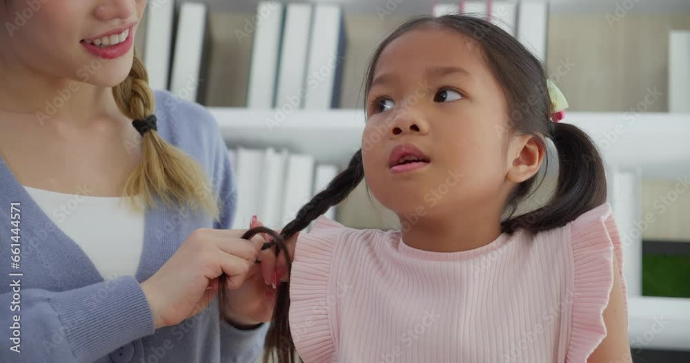 Caring mother braiding pigtail to asian little daughter. Mother braids ...