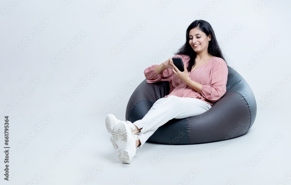 Indian latin female siting on bean bag and browsing on mobile , copy ...