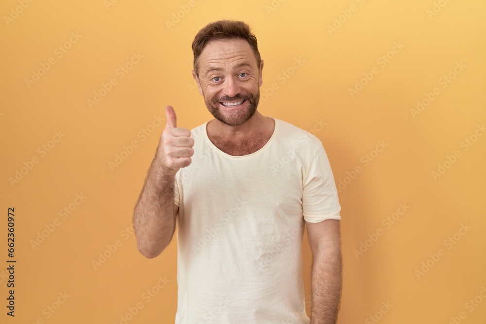 Middle age man with beard standing over yellow background doing happy ...