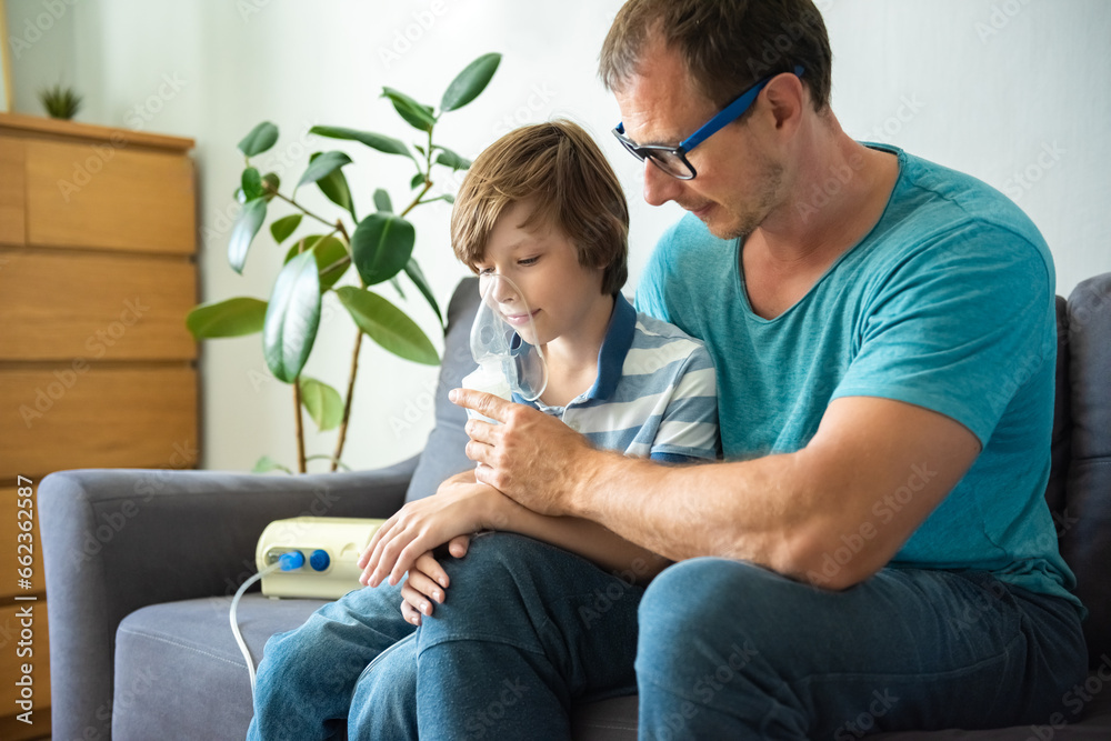Father helps his child boy to makes inhalation at home. Young man with ...