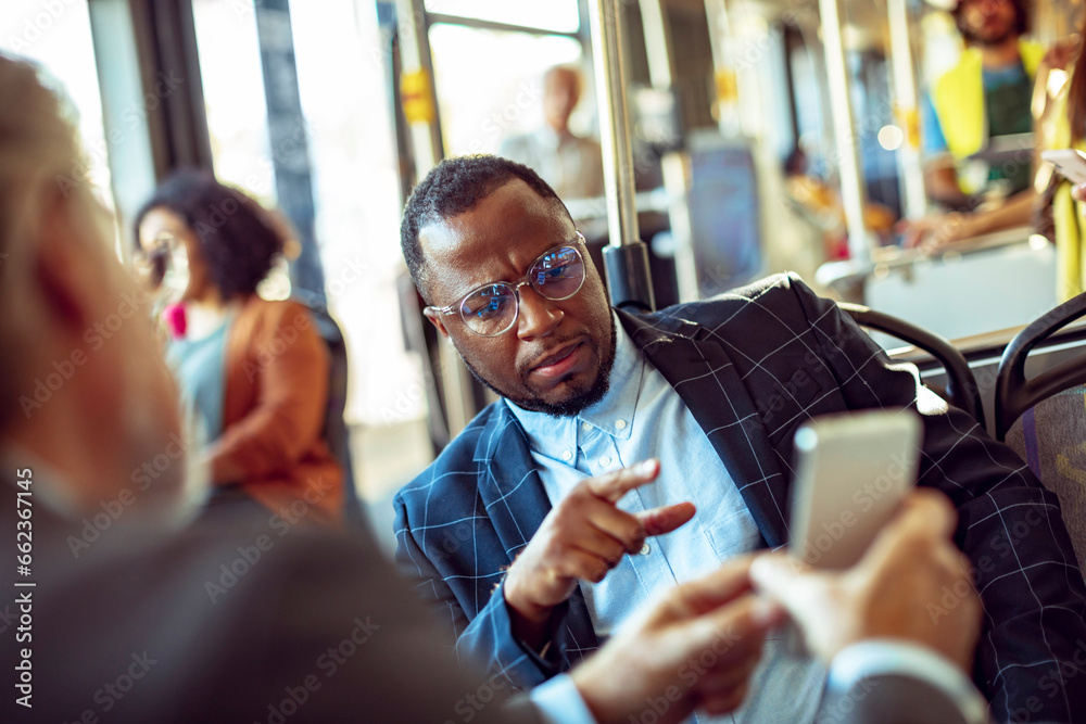 Young businessman pointing on a smartphone of his colleague while ...