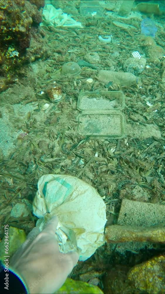 Vertical video, Man dives underwater picks up plastic bag and unties ...