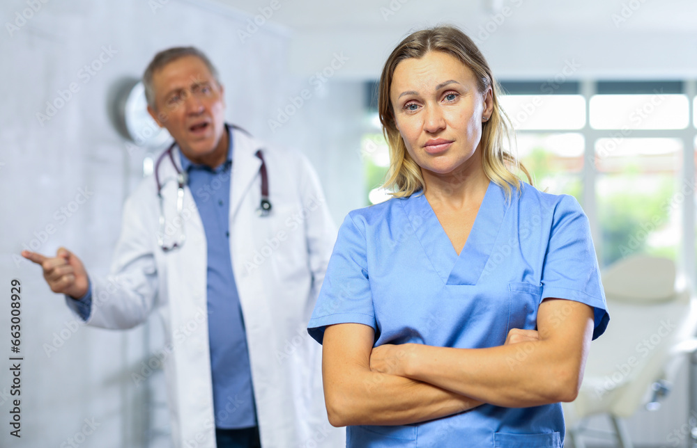 Elderly male doctor and adult female nurse arguing in medical office ...