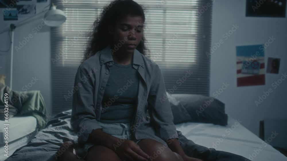 Vídeo do Stock: Zoom in shot of teenage black girl sitting on bed at night, typing on mobile ...