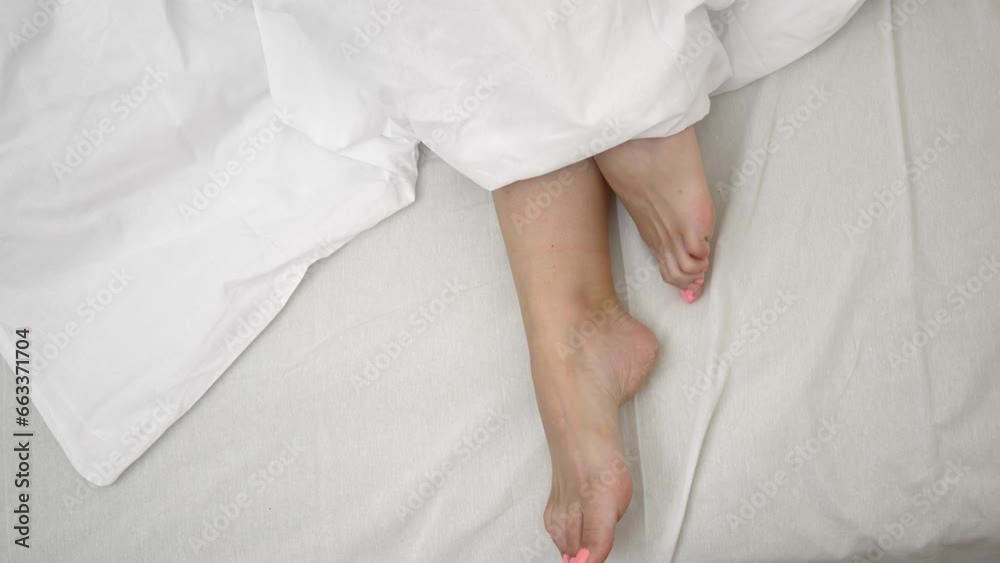 From above, a woman pulling blanket stretching legs in bed joyfully ...
