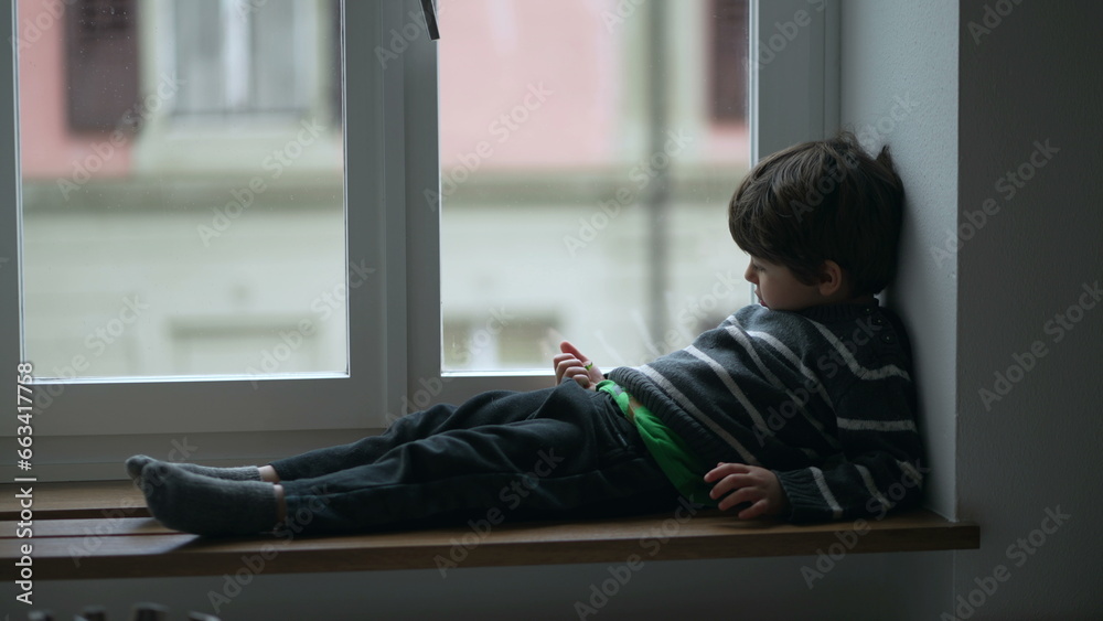 Lazy child sliding down by apartment window, candid bored kid at home ...