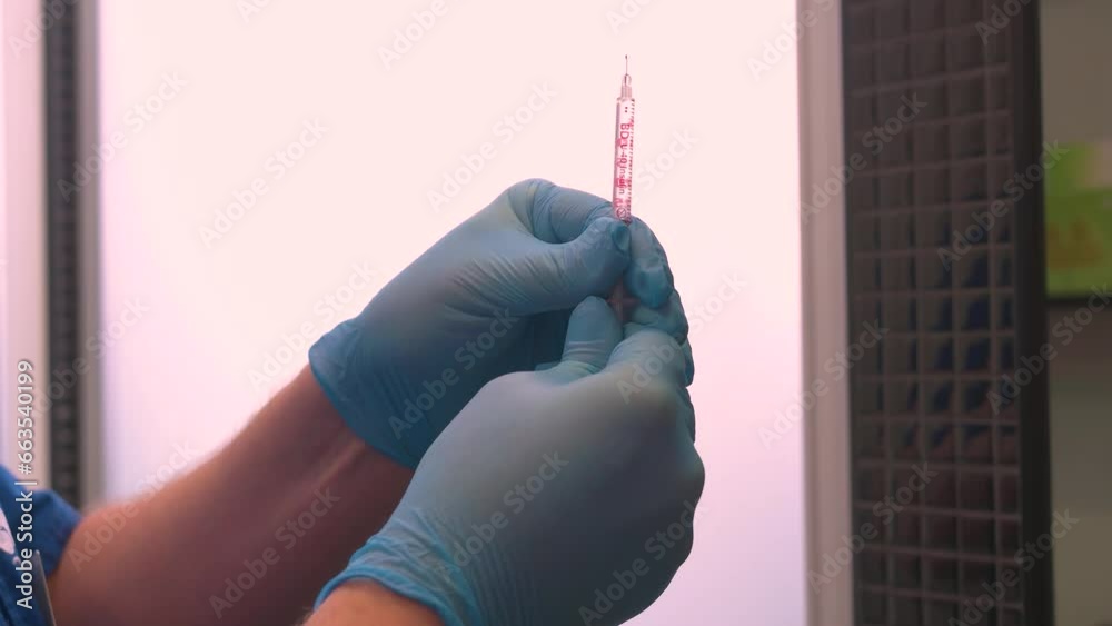 gloved doctor prepares a filled syringe for injection by tapping the ...
