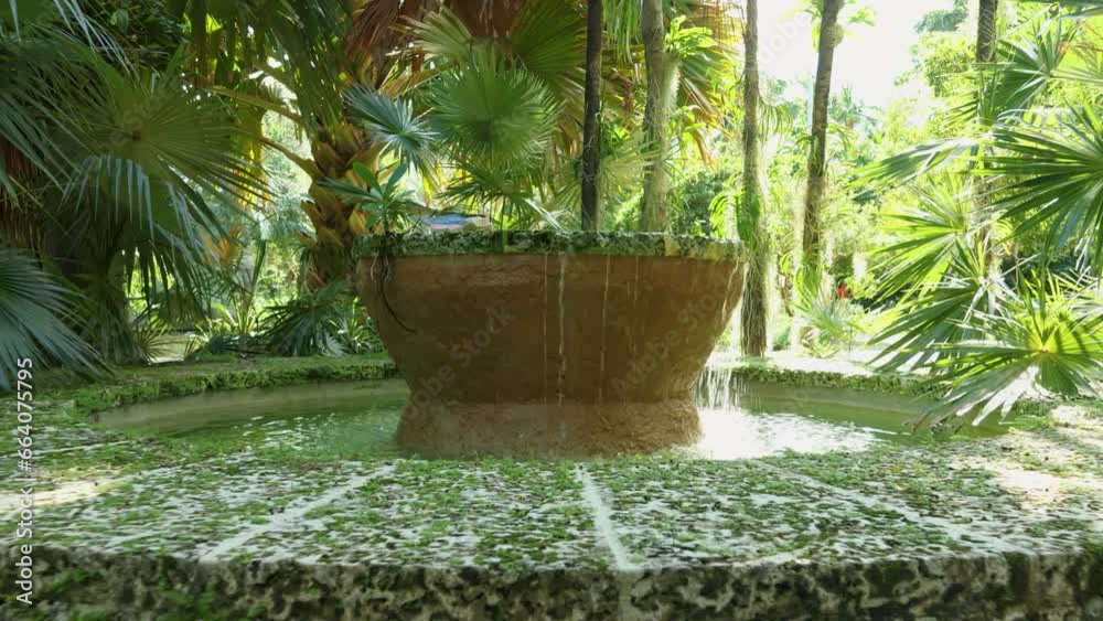 pull out footage of a circular stone water fountain surrounded by lush ...