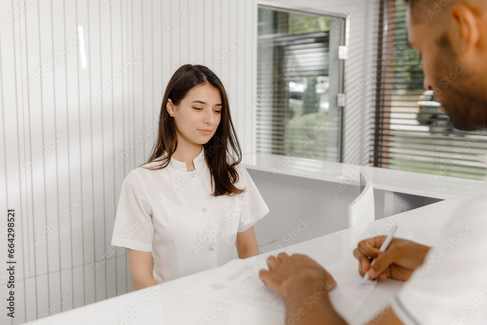 Attractive young medical assistant at reception desk discussing with ...