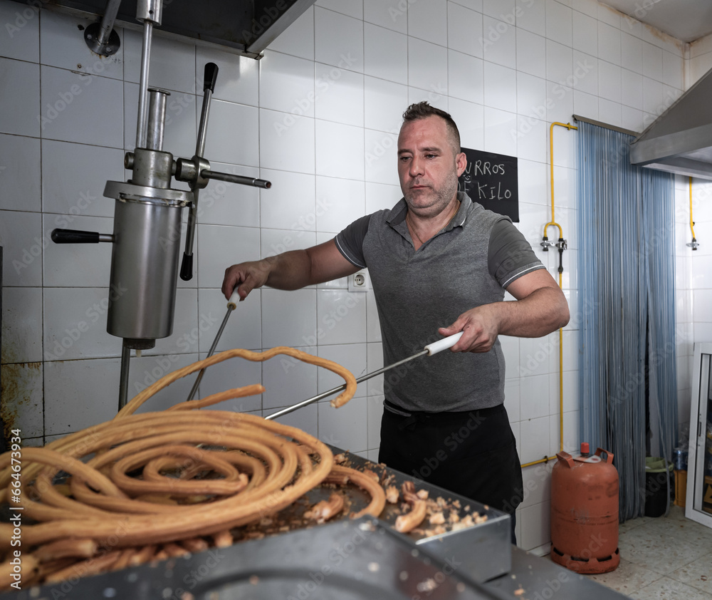 Cocinero sacando masa frita con los palos de churrero para hacer los ...