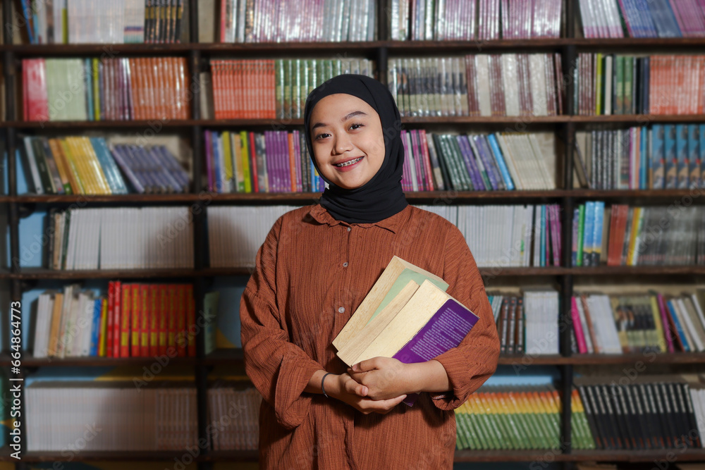 Portrait of Asian hijab woman holding book in front of library ...