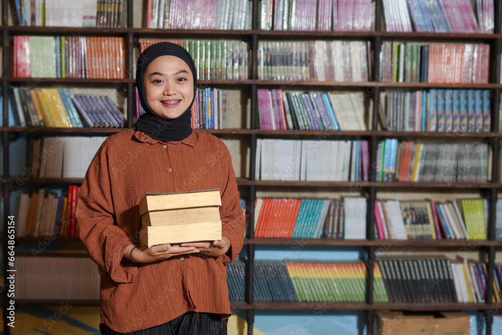 Portrait of Asian hijab woman holding book in front of library ...