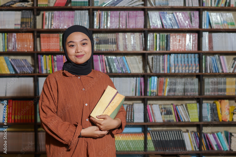 Portrait of Asian hijab woman holding book in front of library ...
