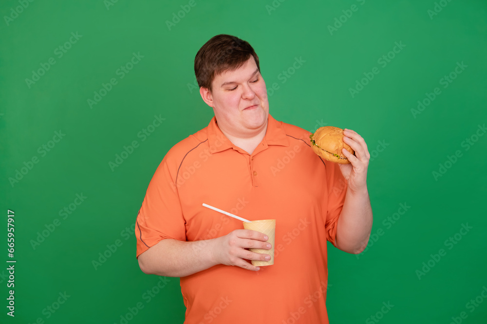Portrait of a fat guy eating a big hamburger and drinking soda from a ...