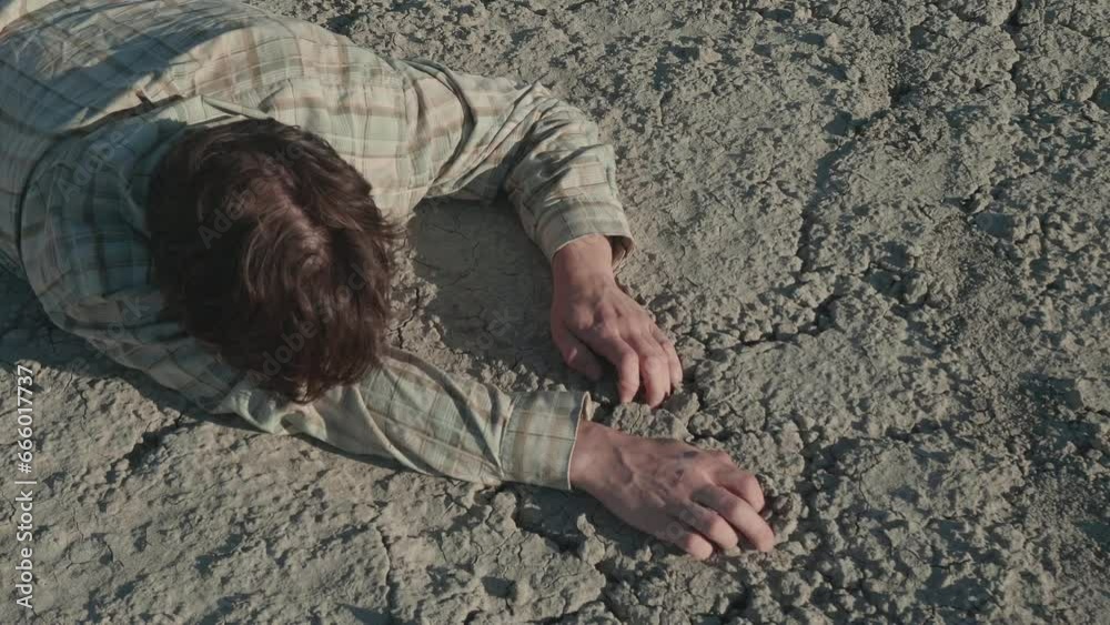 Vidéo Stock An exhausted young man lies on the lifeless ground under ...