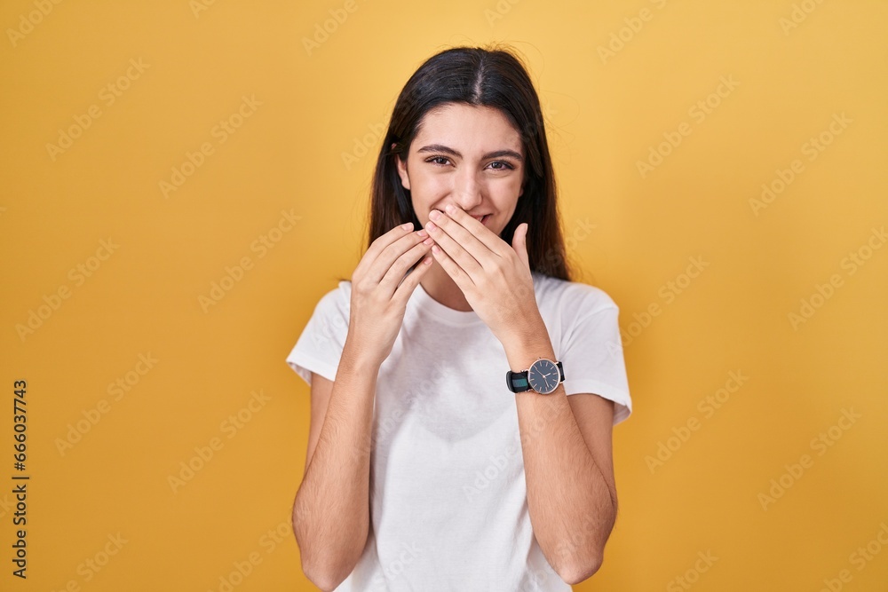 Young beautiful woman standing over yellow background laughing and ...
