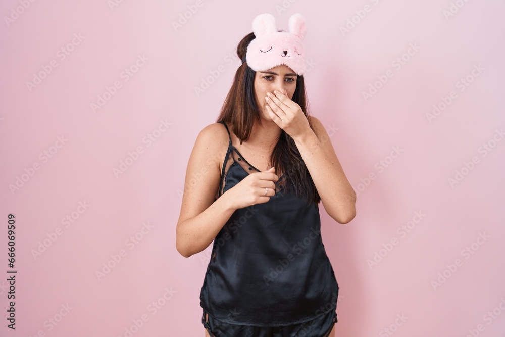 Young brunette woman wearing sleep mask and pyjama smelling something ...