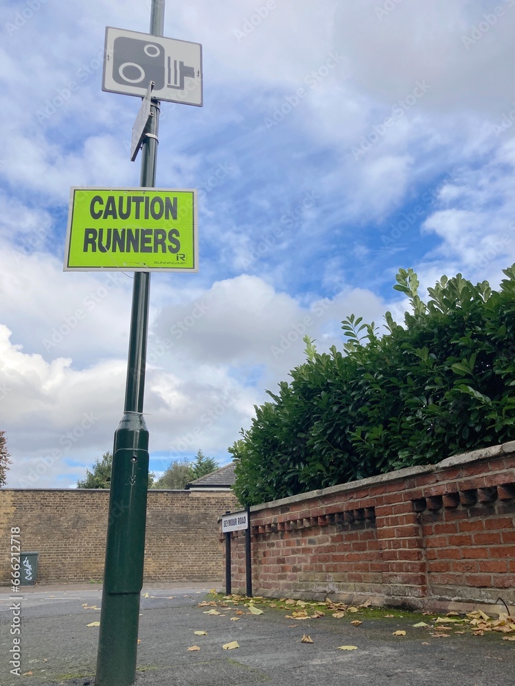 Caution runners sign post on a lamp post on a leafy residential street ...