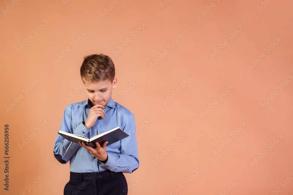 Handsome schoolboy model in blue shirt reading book at beige background ...