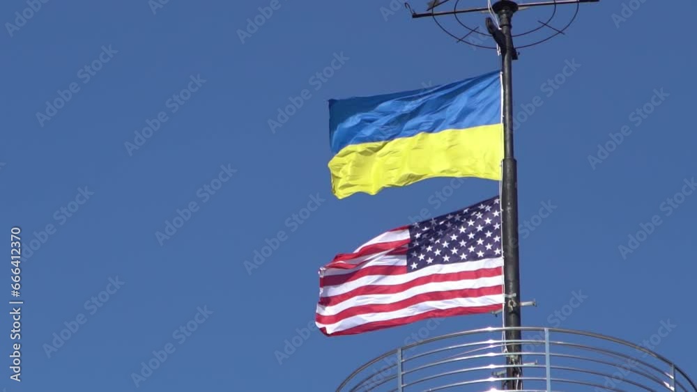 The flags of Ukraine and the USA flutter on a flagpole against a blue ...