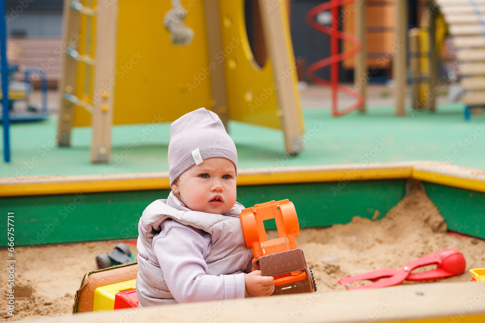 A little girl baby kid playing in the sandbox at the playground ...