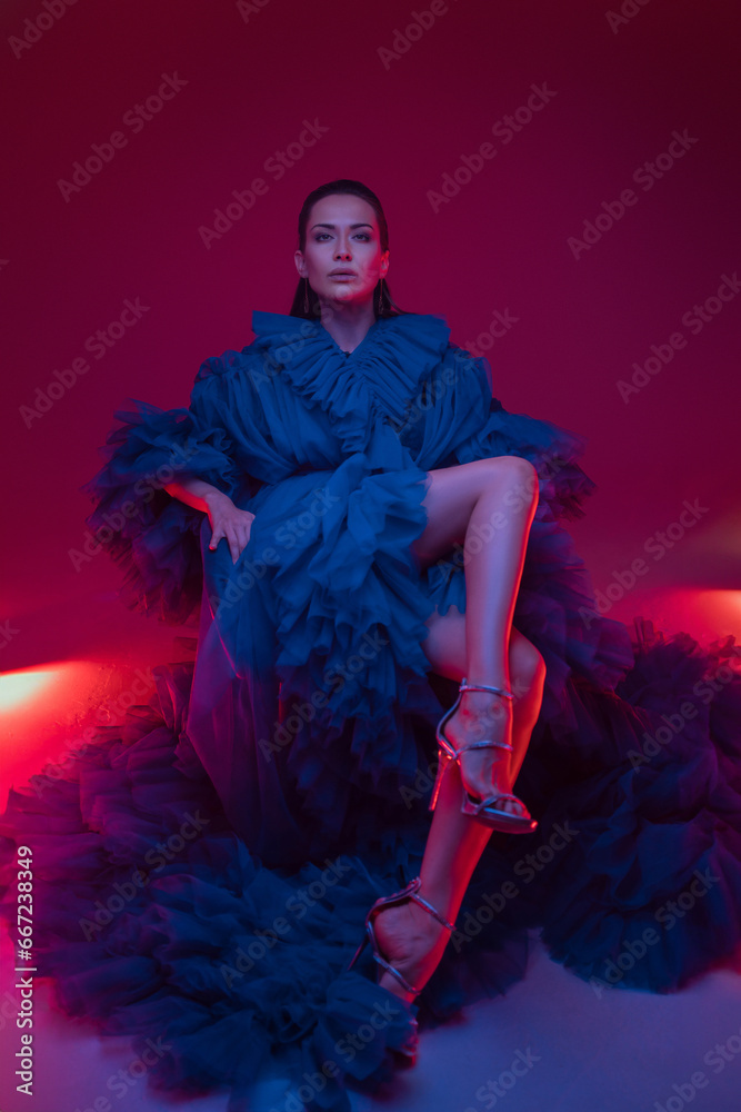Beautiful model in a lavish blue carnival gown poses in a warmly lit ...