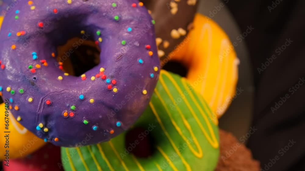 Assorted donuts of different colors rotate at black background close up ...