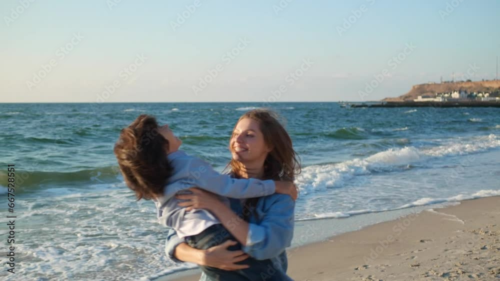 Little boy running to hug his mother on beach. Young woman catching her ...