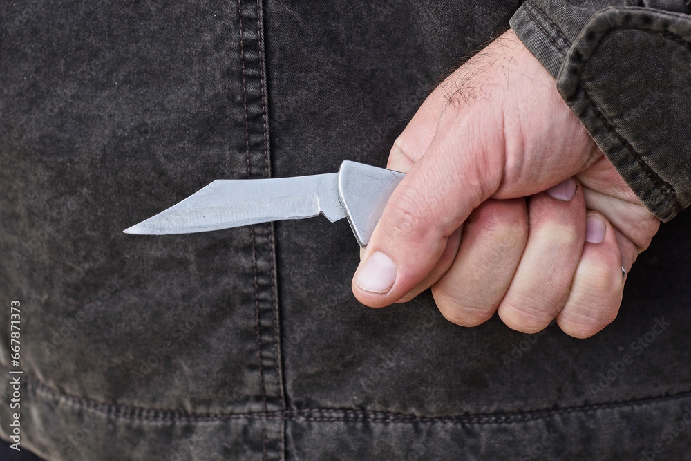 hand of a male criminal in black clothes and a gray knife behind his ...
