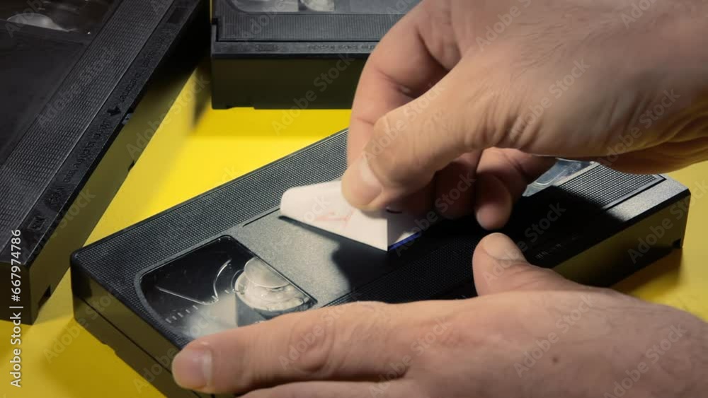 A hand applies a handwritten label to a VHS tape, with the text 1980s ...