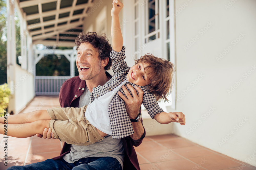 Joyful father playfully lifting his laughing son in the air on a sunny ...