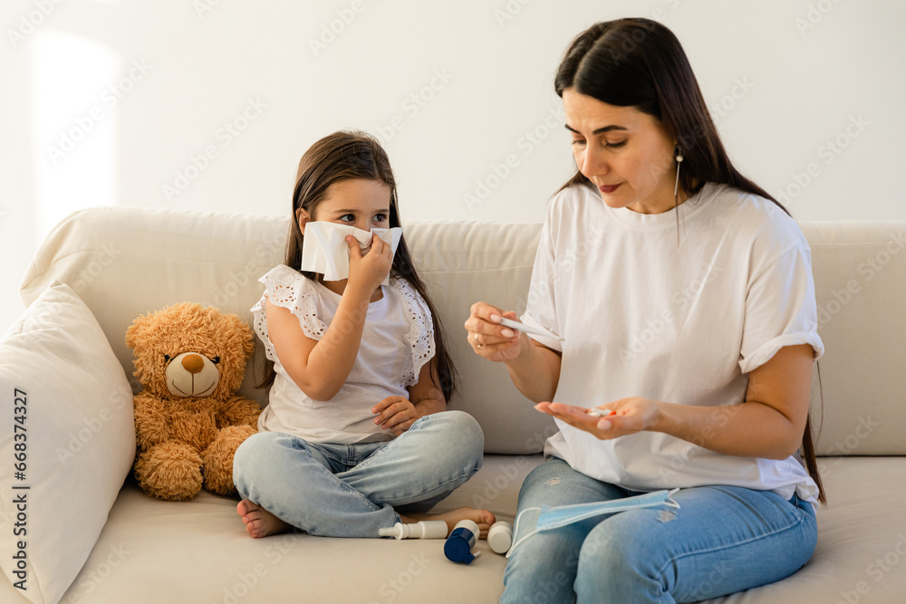 Worried mom treating sick kid suffering from flu and fever, holding thermometer, checking high ...