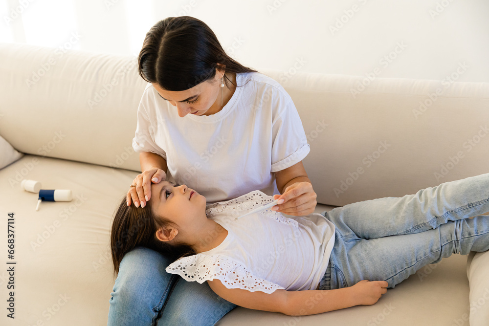 Sad little girl laying on sofa, feeling ill, complaining her mom, expecting mother checking her ...