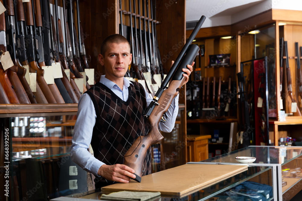 Gun shop salesman standing behind counter and showing modern sporting ...