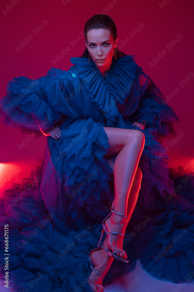 Beautiful model in a lavish blue carnival gown poses in a warmly lit ...