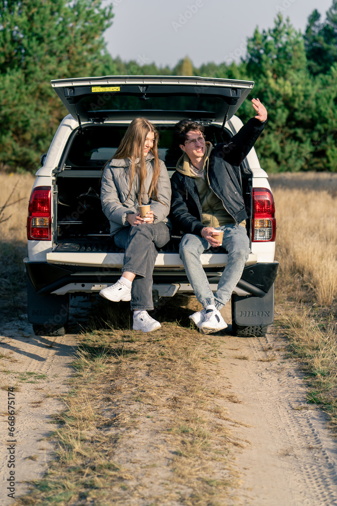 A guy and a girl are sitting together in the open trunk of a crossover ...