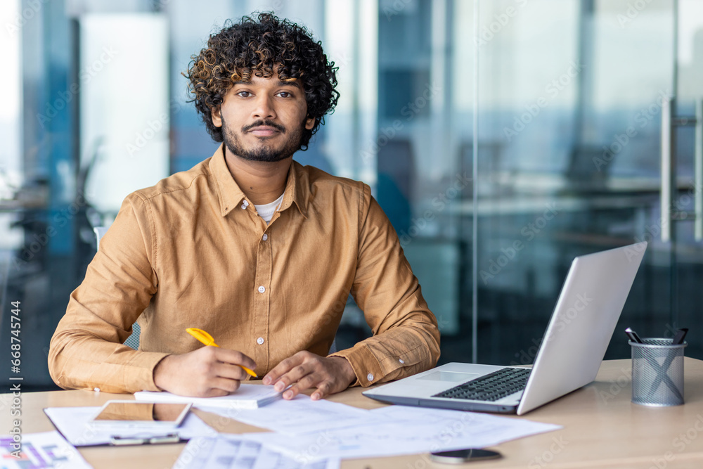 Portrait of young serious thinking businessman inside office behind ...