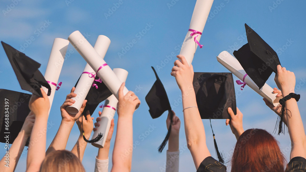 College graduates raise their hands with caps and diplomas to the sky ...